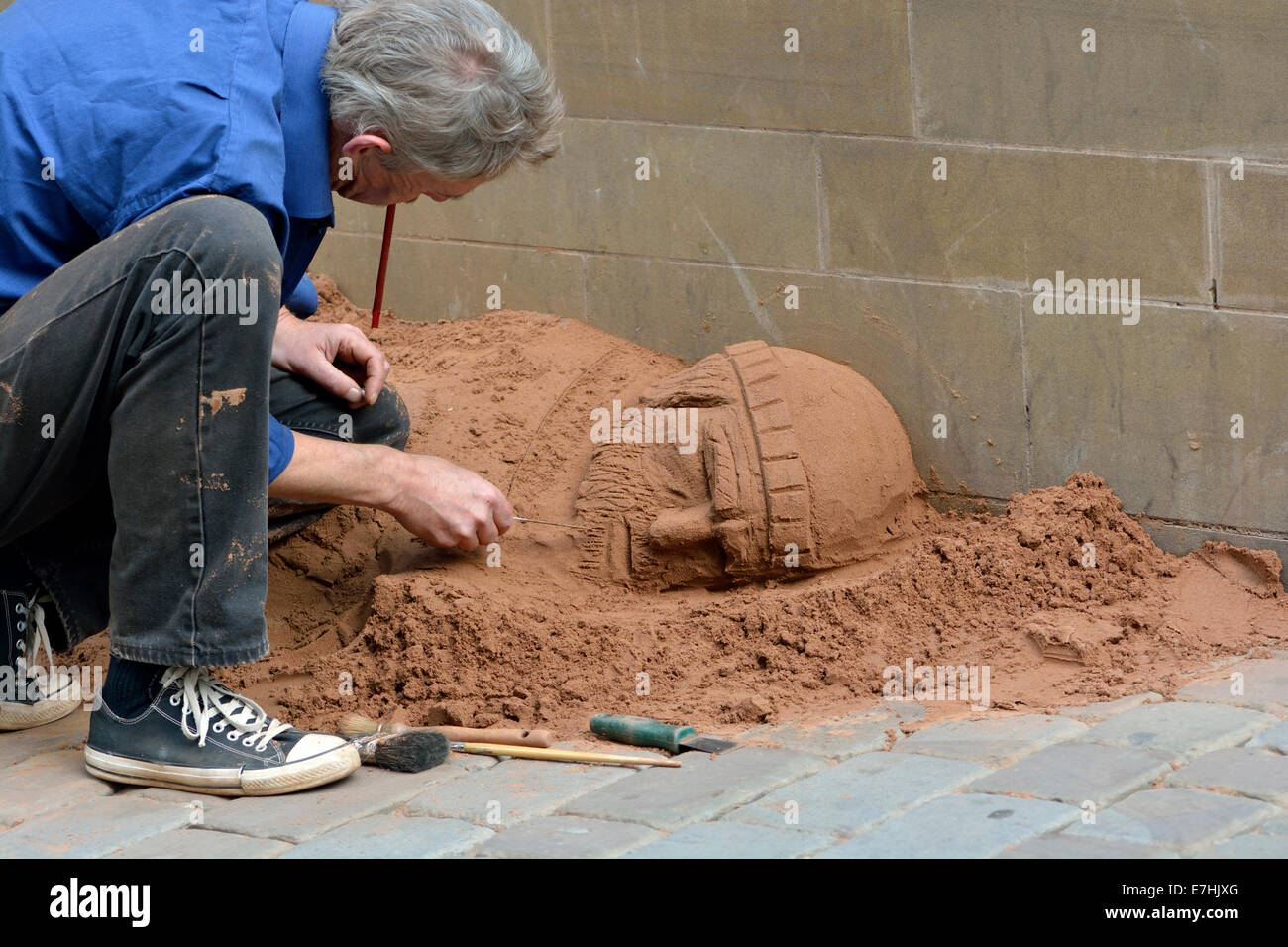 a man sculpts the face of a man out of sand on the pavement in market ...