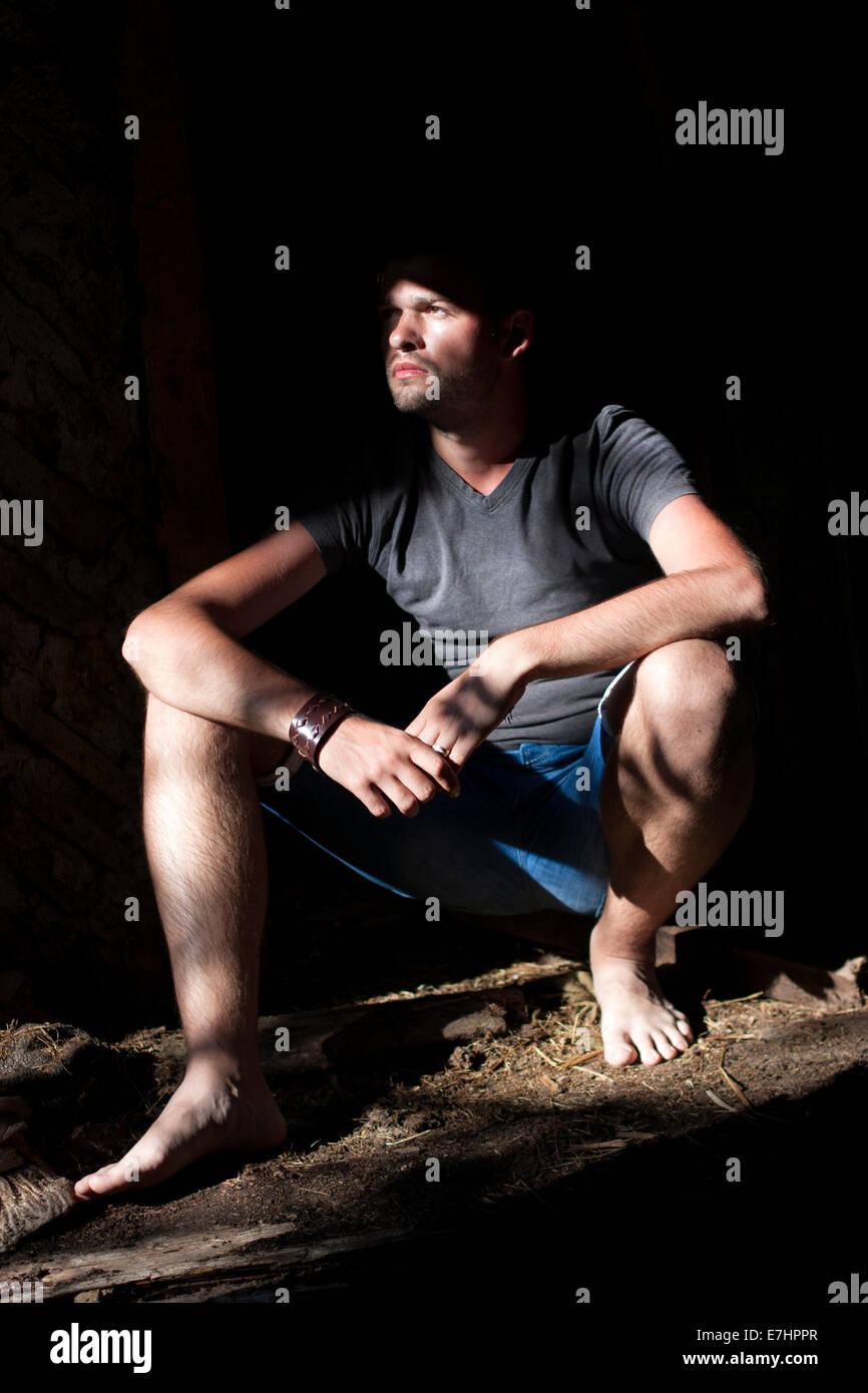 Young man sitting in shadows on hay Stock Photo - Alamy