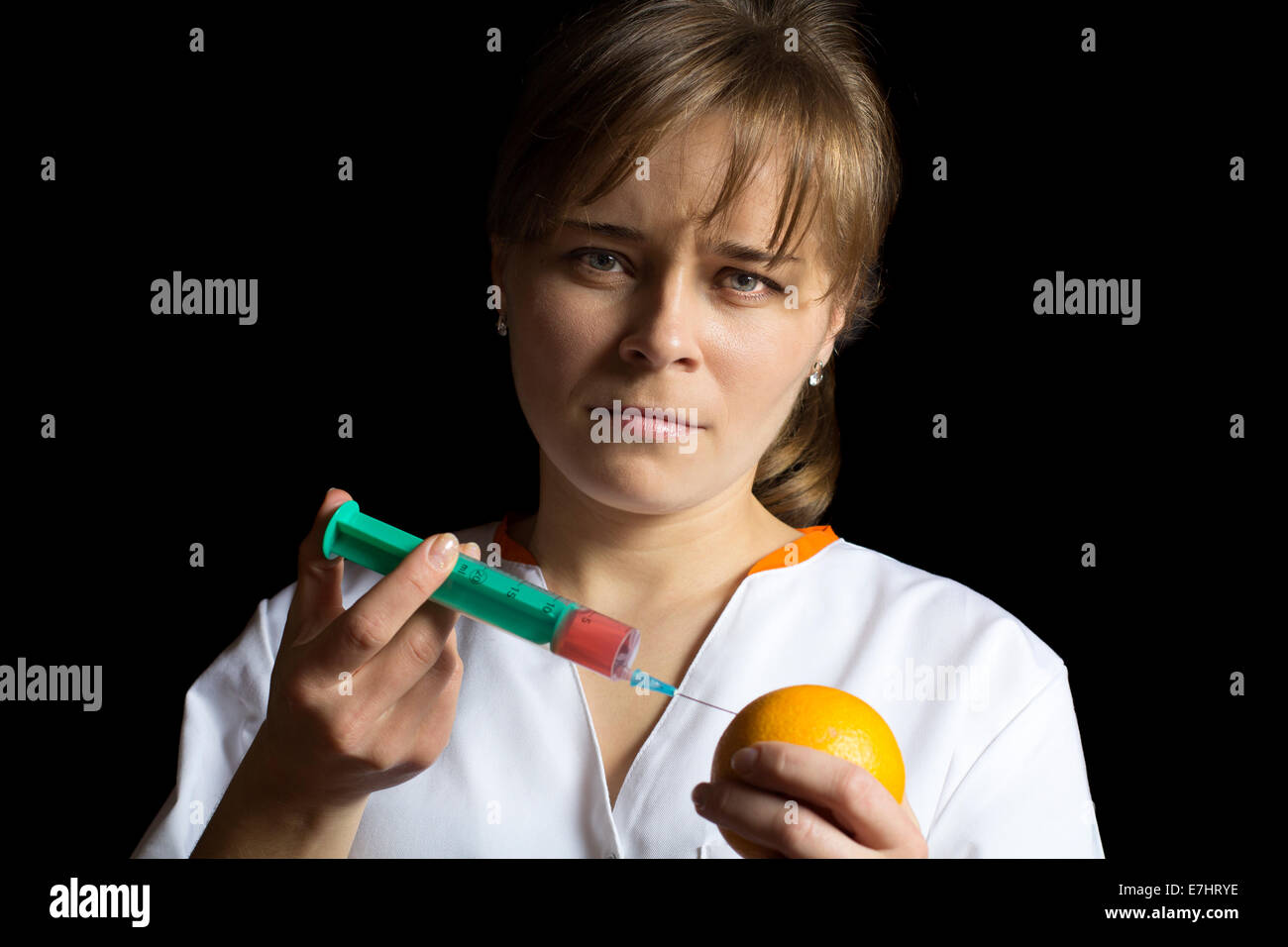 Young woman injecting orange fruit with syringe isolated on black Stock ...