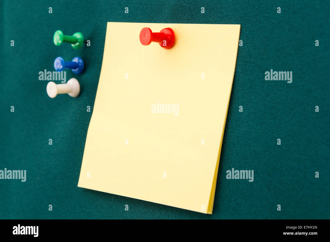 Yellow post-it note with red push pin on a green board Stock Photo - Alamy