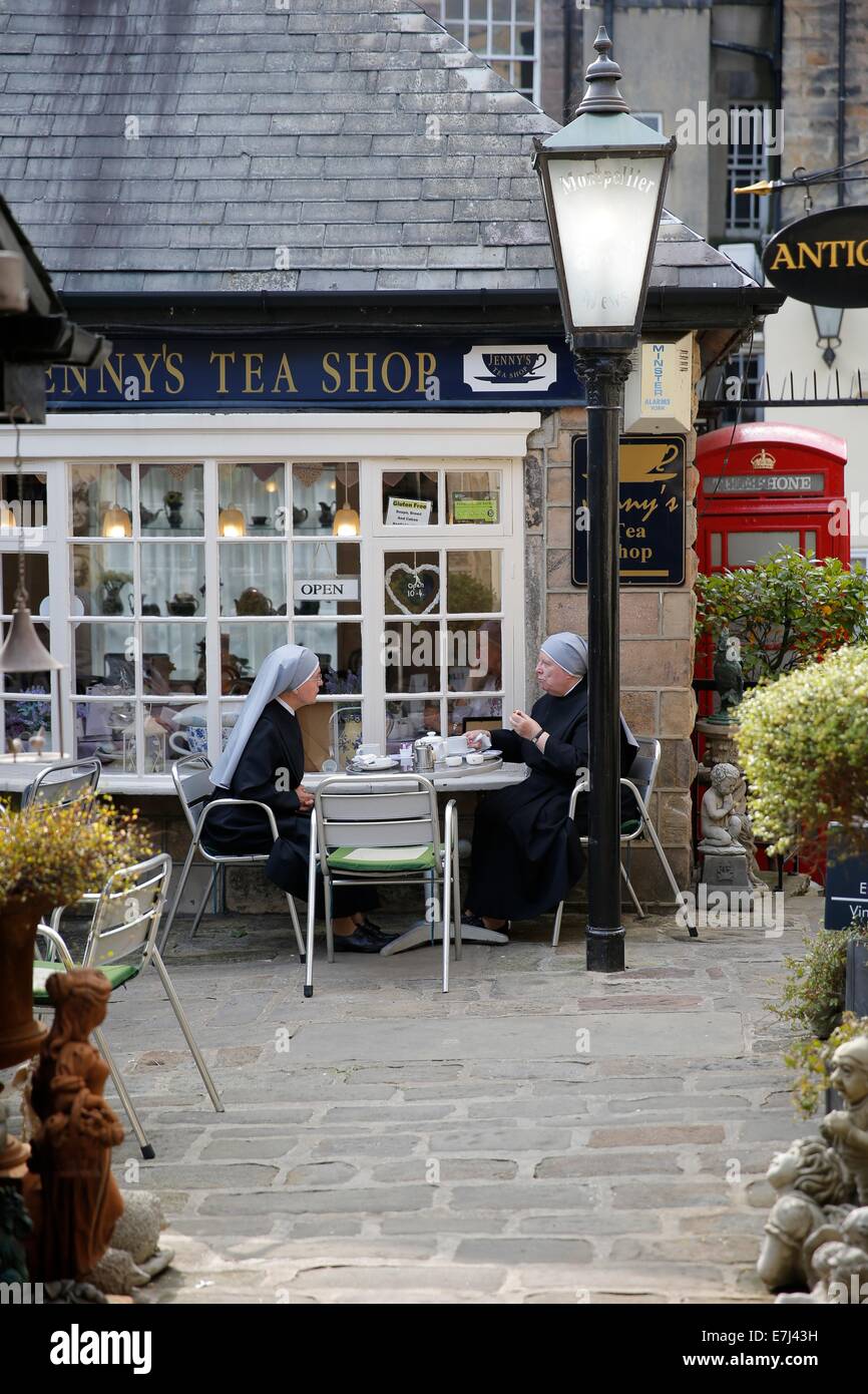 Two nuns sat enjoying tea at the café with lady walking through arch ...