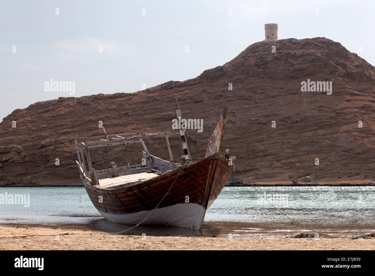 Dhow-ship in the harbour of Sur, in front of a rocky hill with a ...