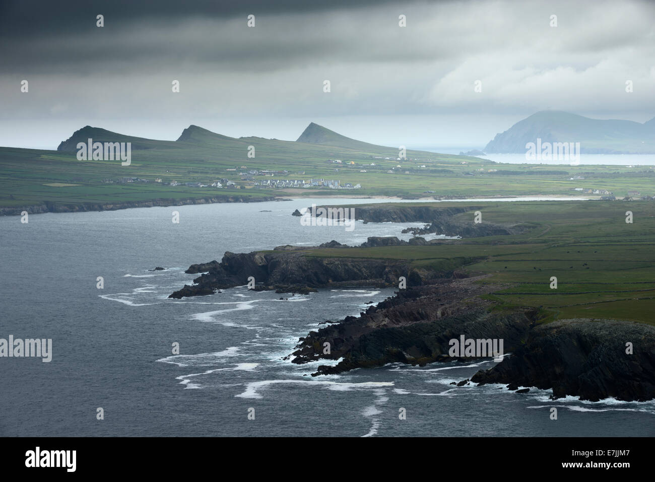 Dark clouds loom over Ballyferriter Bay and the peaks of the Three ...