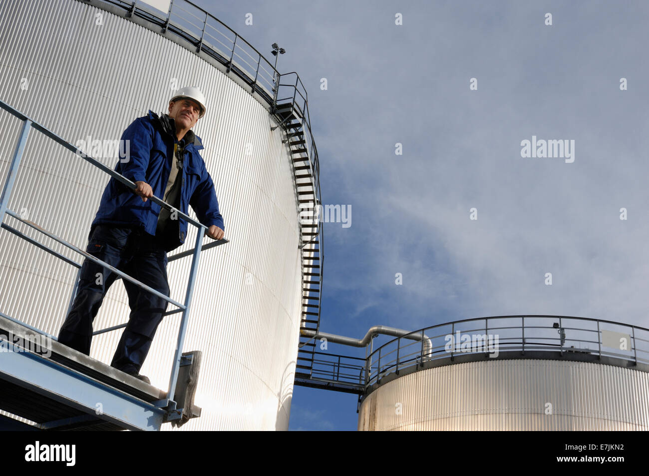 oil worker, engineer, with giant fuel storage towers in background ...