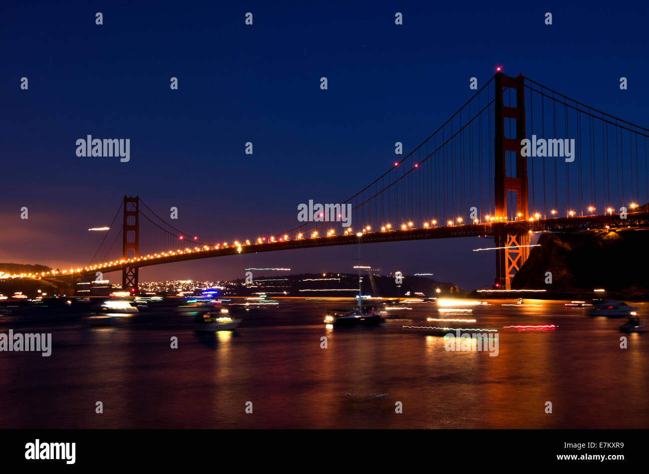Golden Gate Bridge at dusk, boats with streaked lights hove-to below it ...