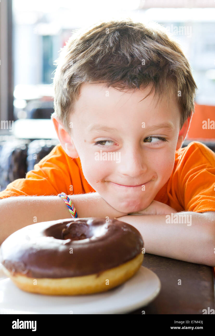 A young boy looking at a chocolate donut Stock Photo - Alamy