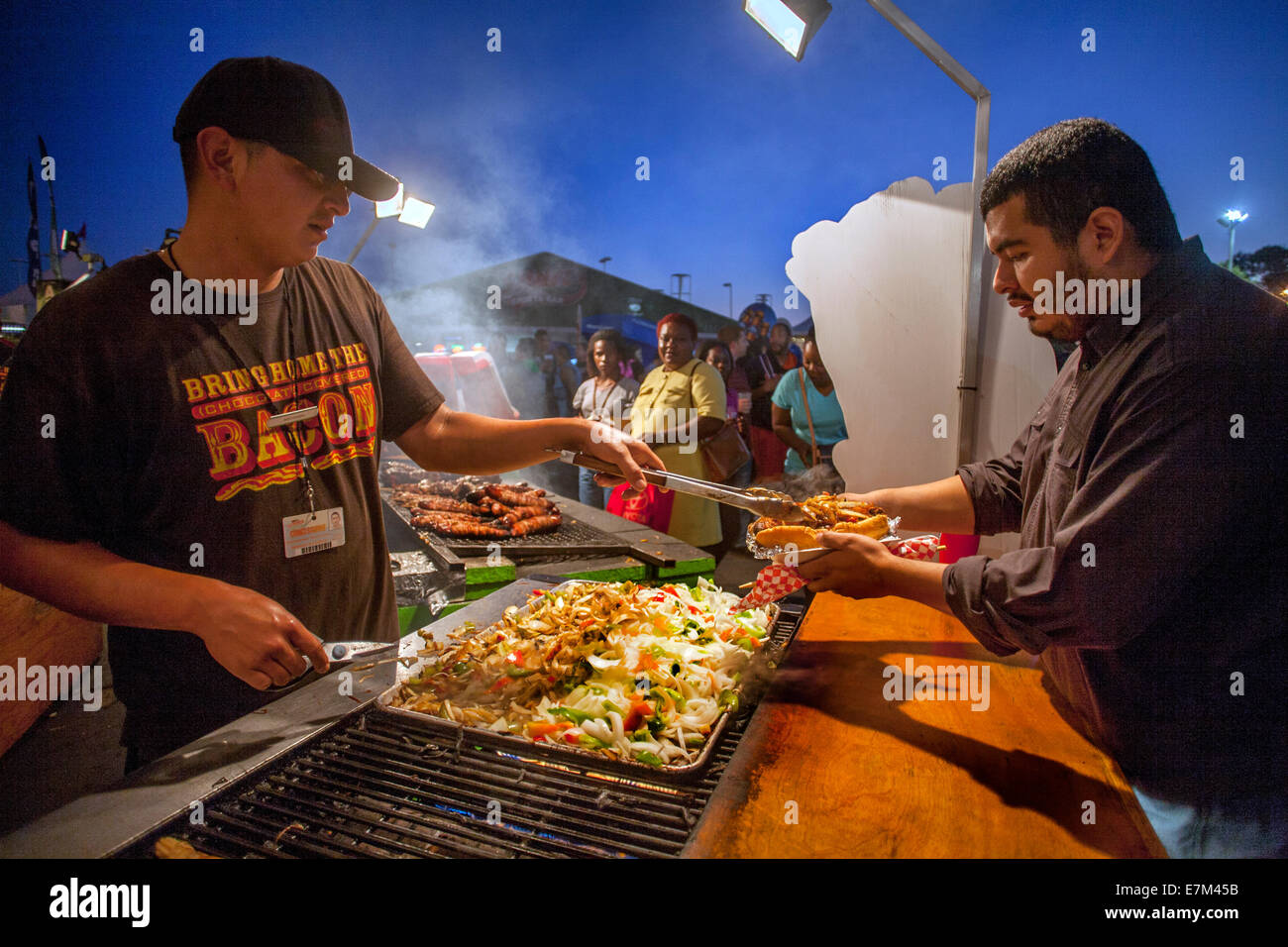 A Hispanic customer buys a grilled sausage and vegetables from a fast ...
