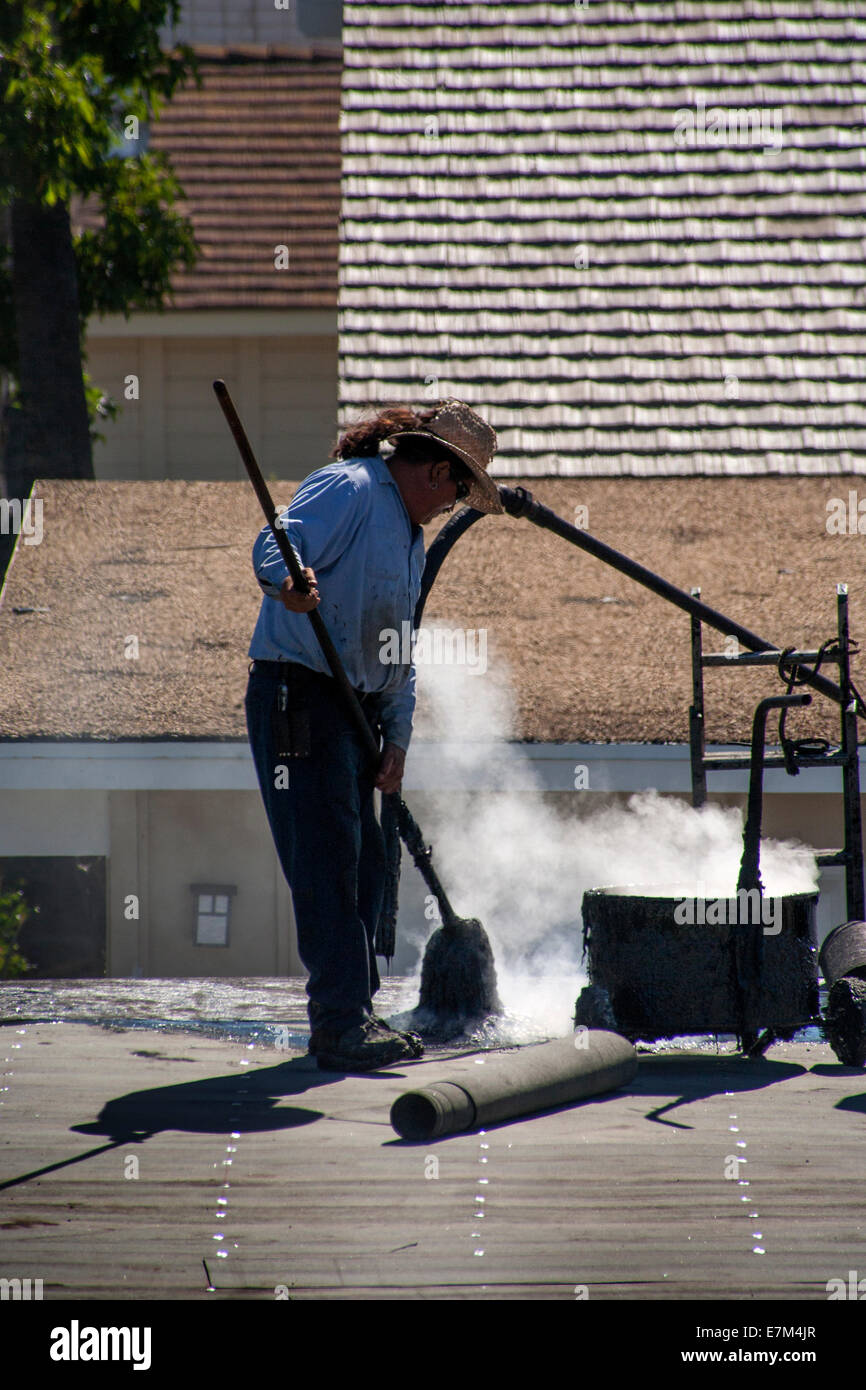 Steam rises from mopping hot tar as a a Hispanic workmen replaces a ...