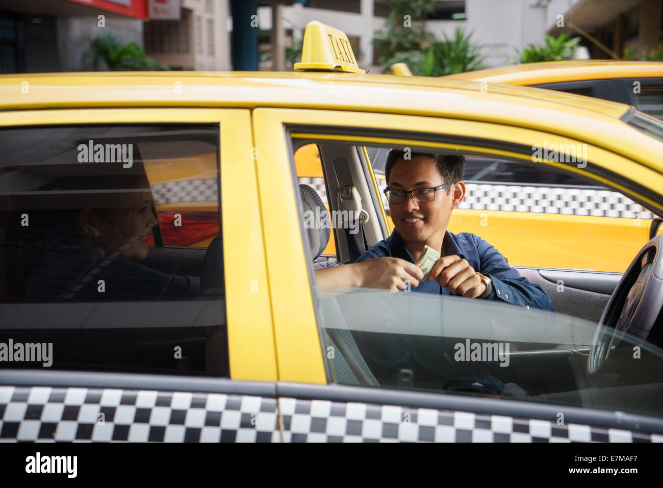Asian man working as taxi driver in yellow car, with female client ...