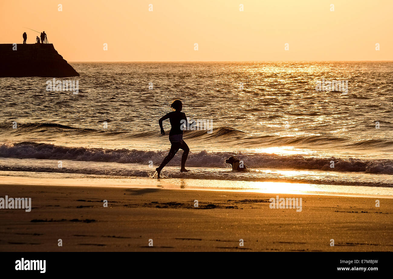 A woman runs into the sea at Sennen Cove at Sunset Stock Photo - Alamy