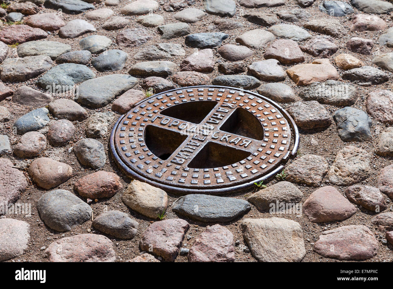 Old steel sewer manhole on the cobblestone road. Text on russian: Urban ...