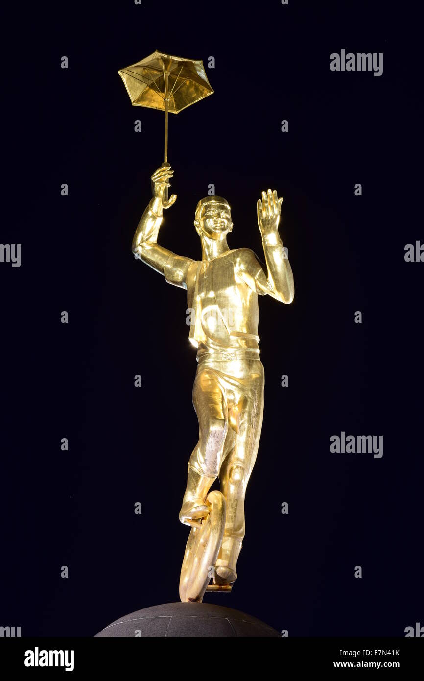 A night view of the gilded statue of a circus man on a wheel with an ...