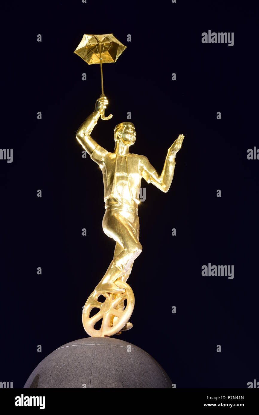 A night view of the gilded statue of a circus man on a wheel with an ...