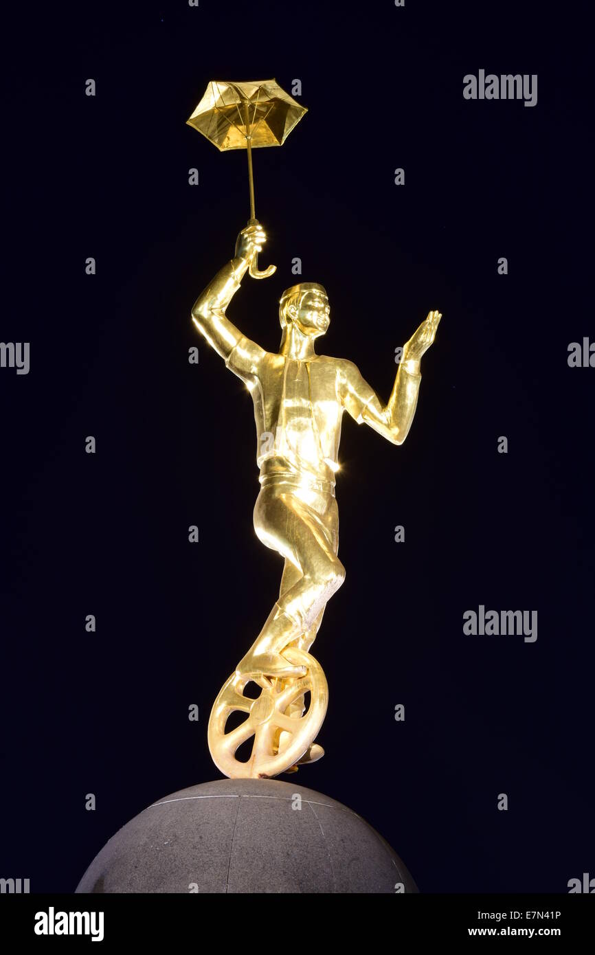 A night view of the gilded statue of a circus man on a wheel with an ...