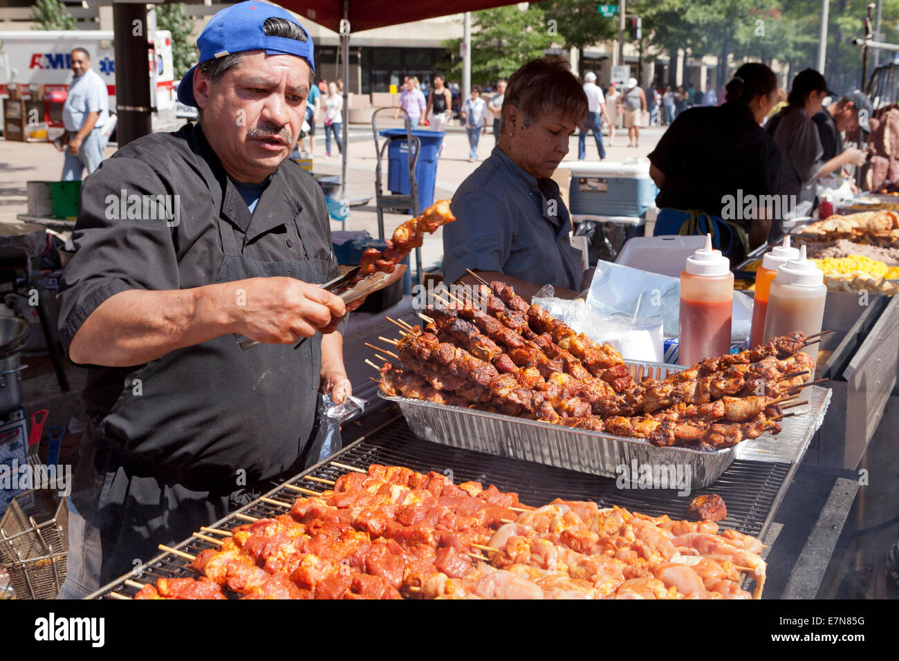 Man grilling chicken skewers on barbecue grill at an outdoor festival ...