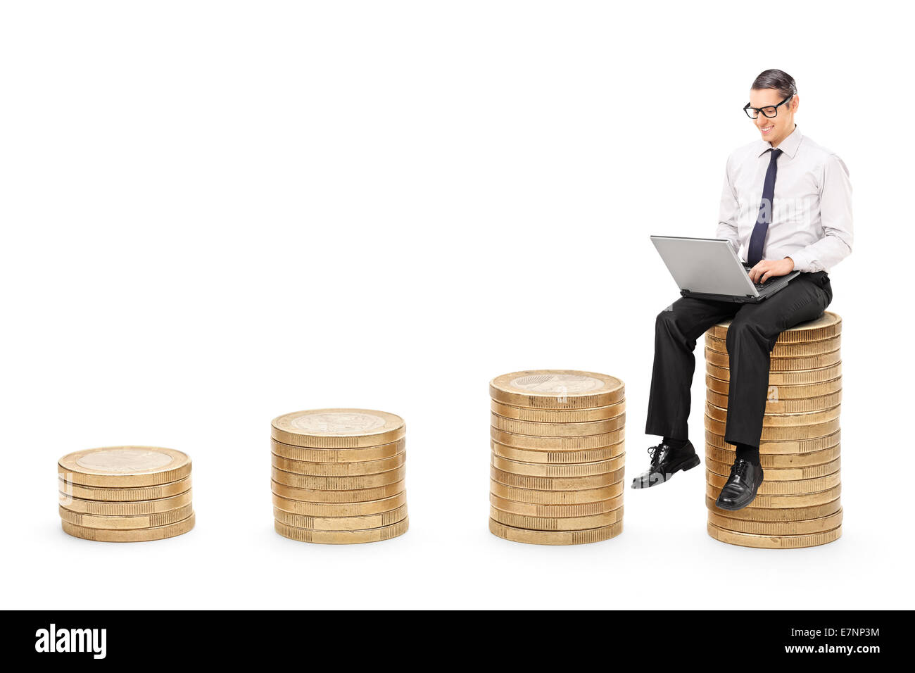 Man working on laptop seated on a stack of coins isolated on white ...