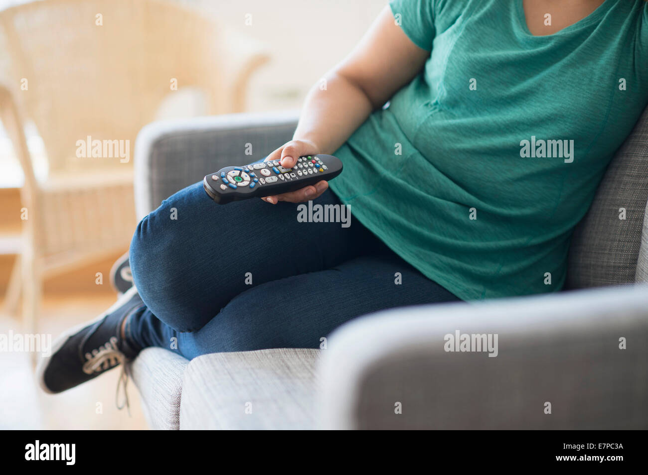 Woman sitting on sofa with remote control Stock Photo - Alamy