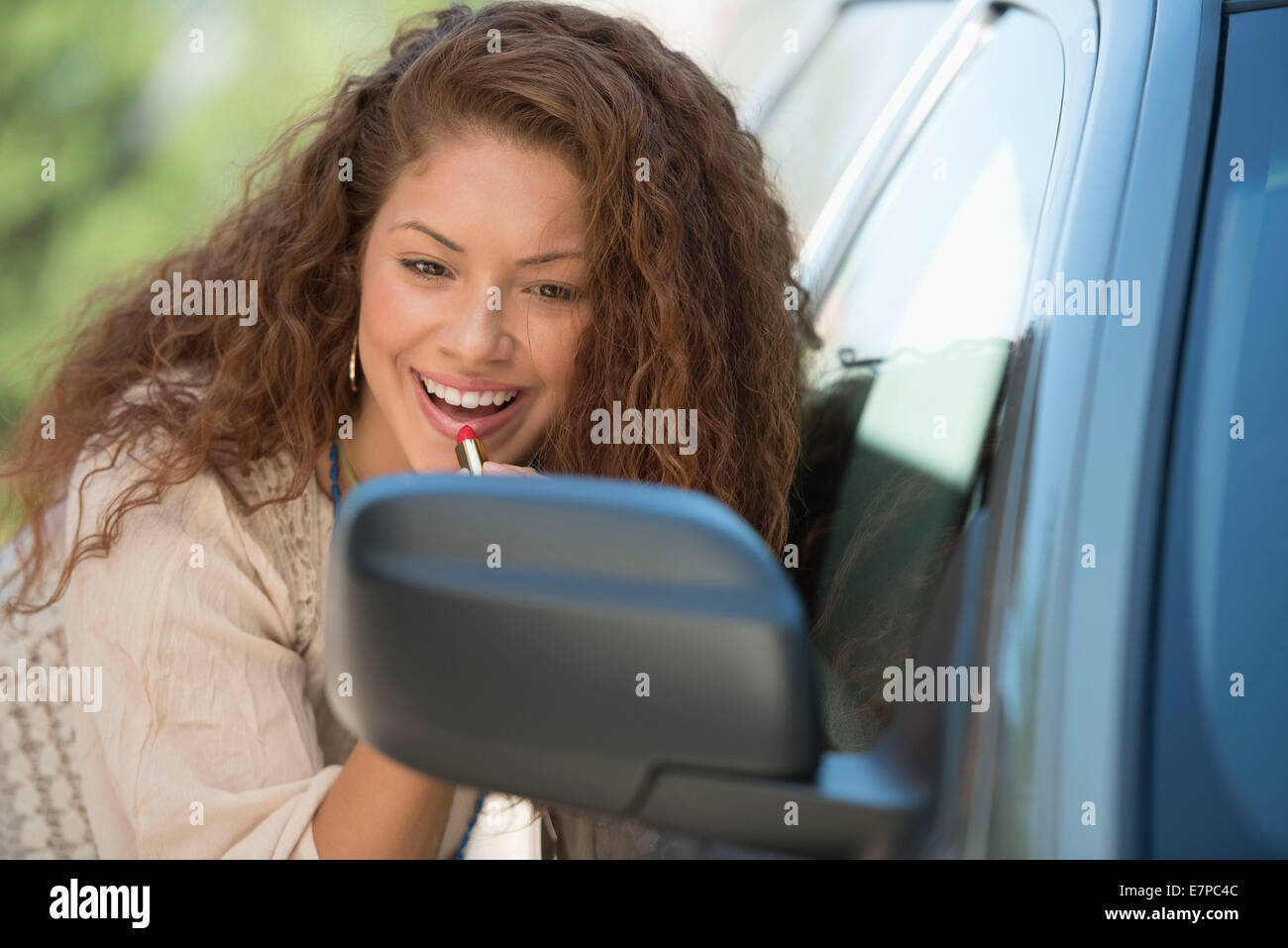 Young woman putting lipstick looking at rear mirror Stock Photo - Alamy