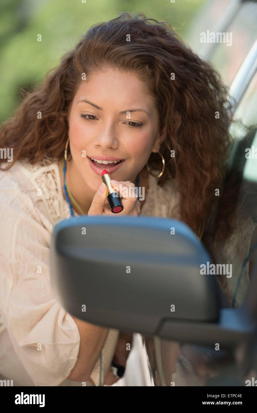 Young woman putting lipstick looking at rear mirror Stock Photo - Alamy