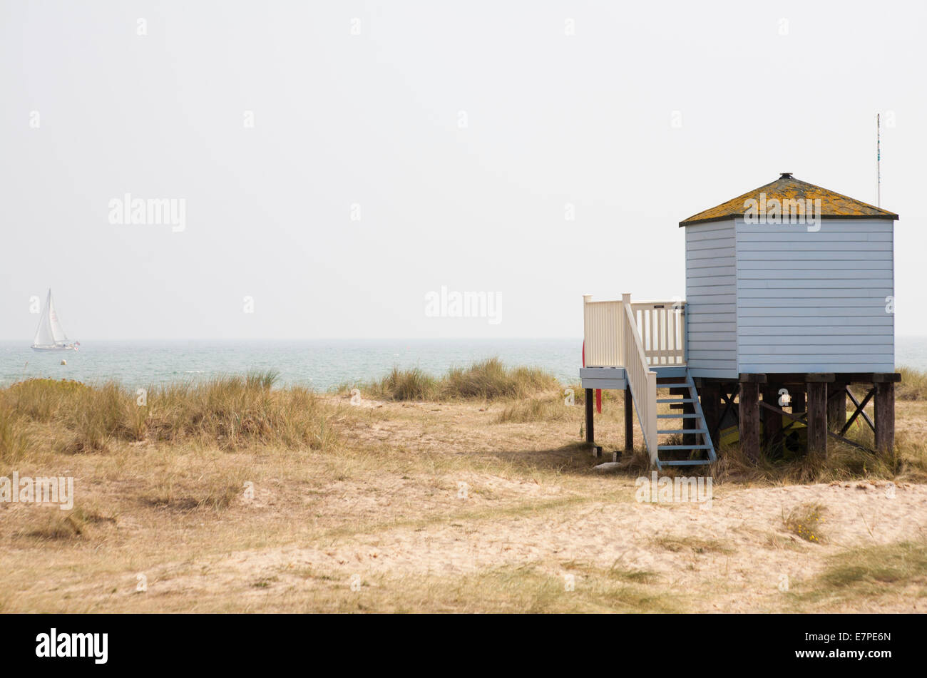 Sand dunes with beach hut raised off the ground and yacht sailing by at ...