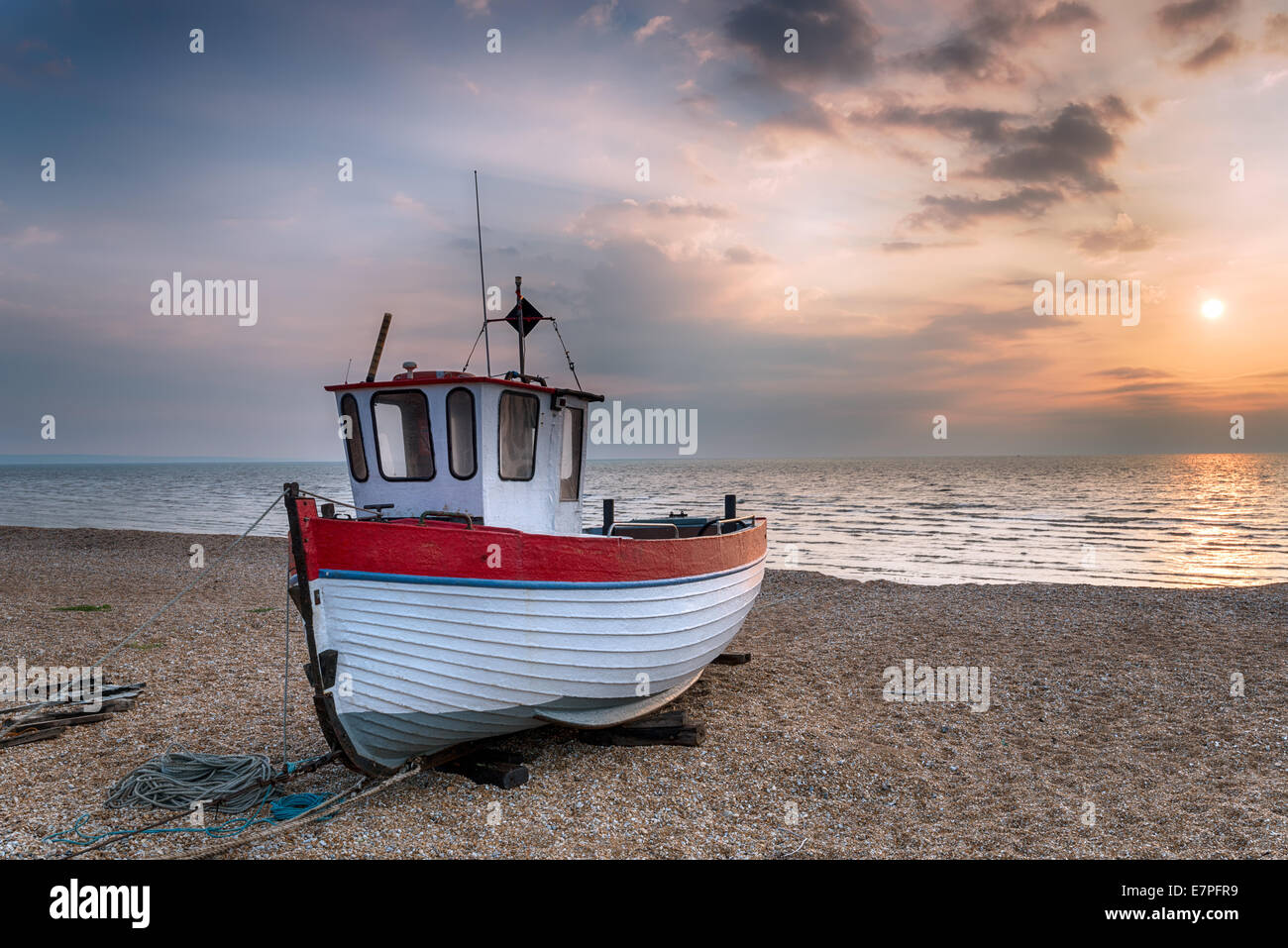 A red and white wooden fishing boat on the beach just after sunrise ...