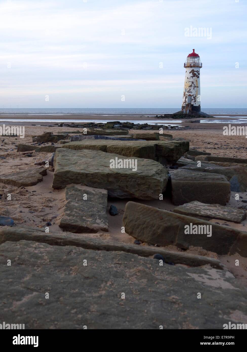 Abandoned lighthouse on the beach with the tide out and rocks in the ...