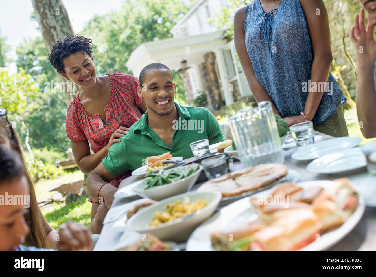 A family gathering, men, women and children around a table in a garden ...
