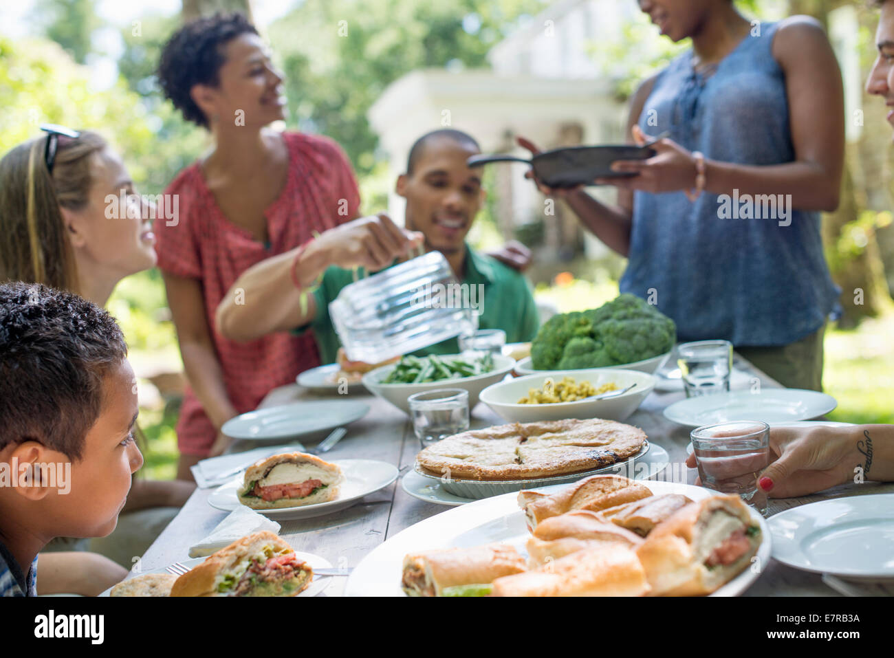 A family gathering, men, women and children around a table in a garden ...