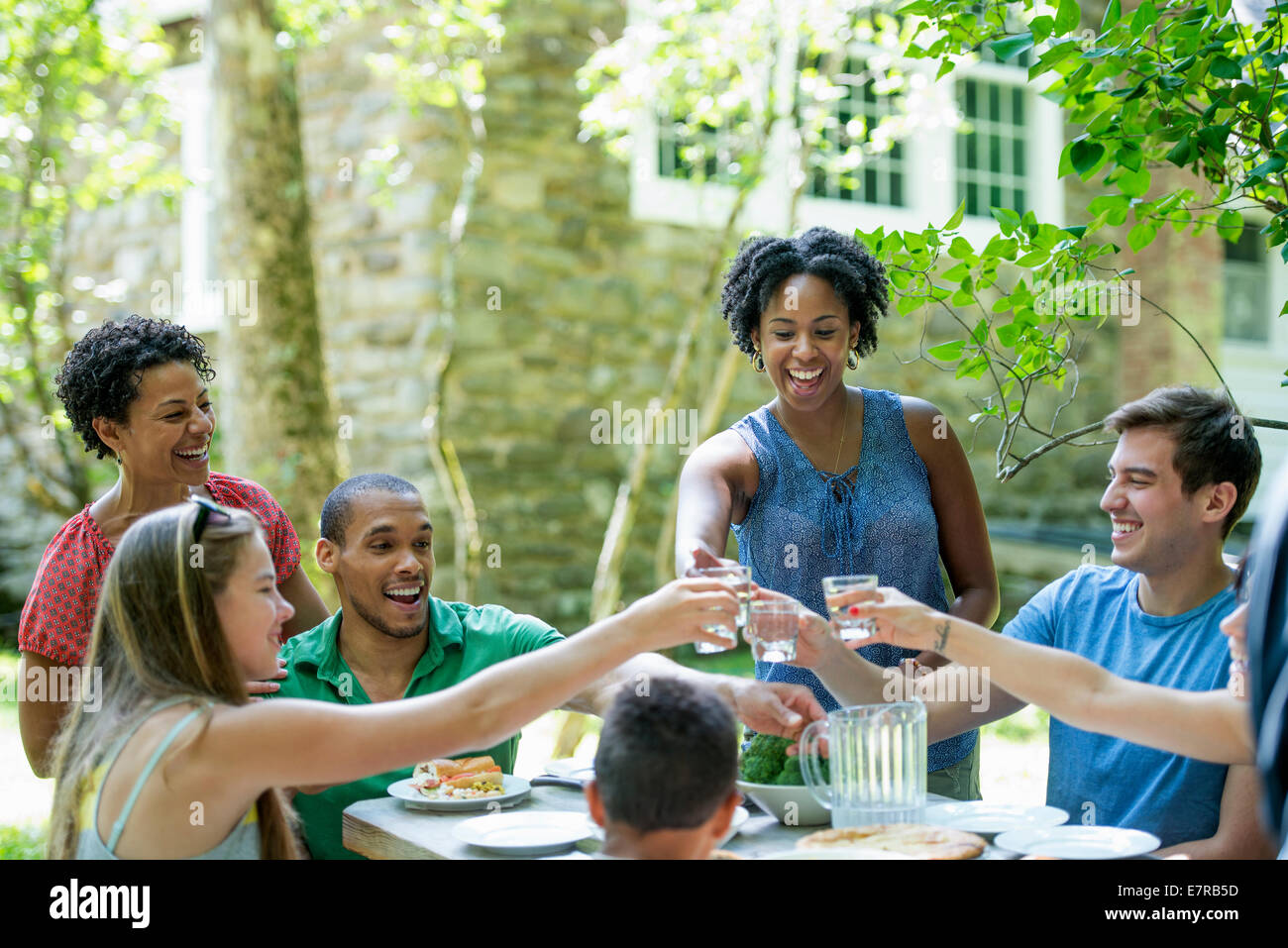 A family gathering, men women and children around a table in a garden ...