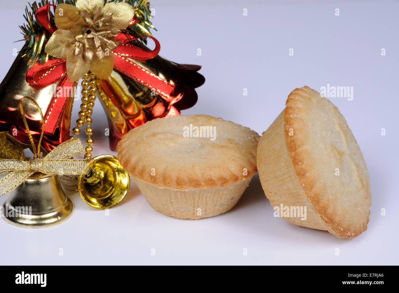 Two mince pies with Christmas bells to the rear against a grey ...