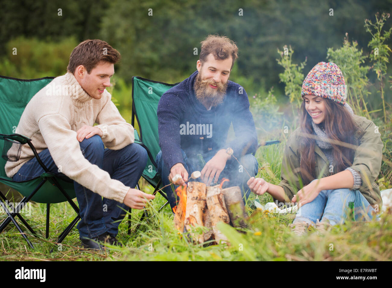 group of smiling friends sitting around bonfire Stock Photo - Alamy