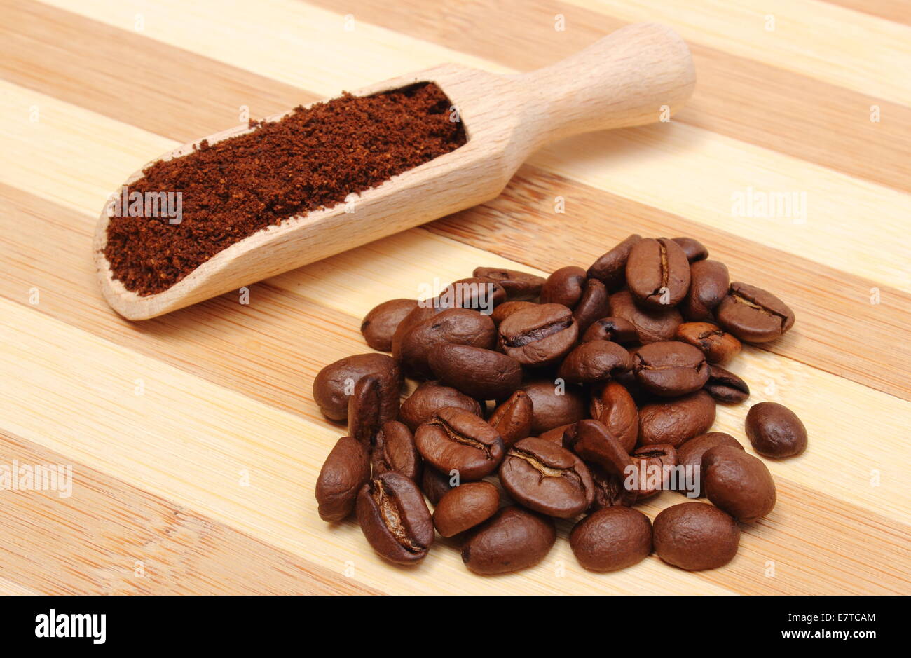 Heap of coffee grains and ground coffee on wooden spoon in background ...