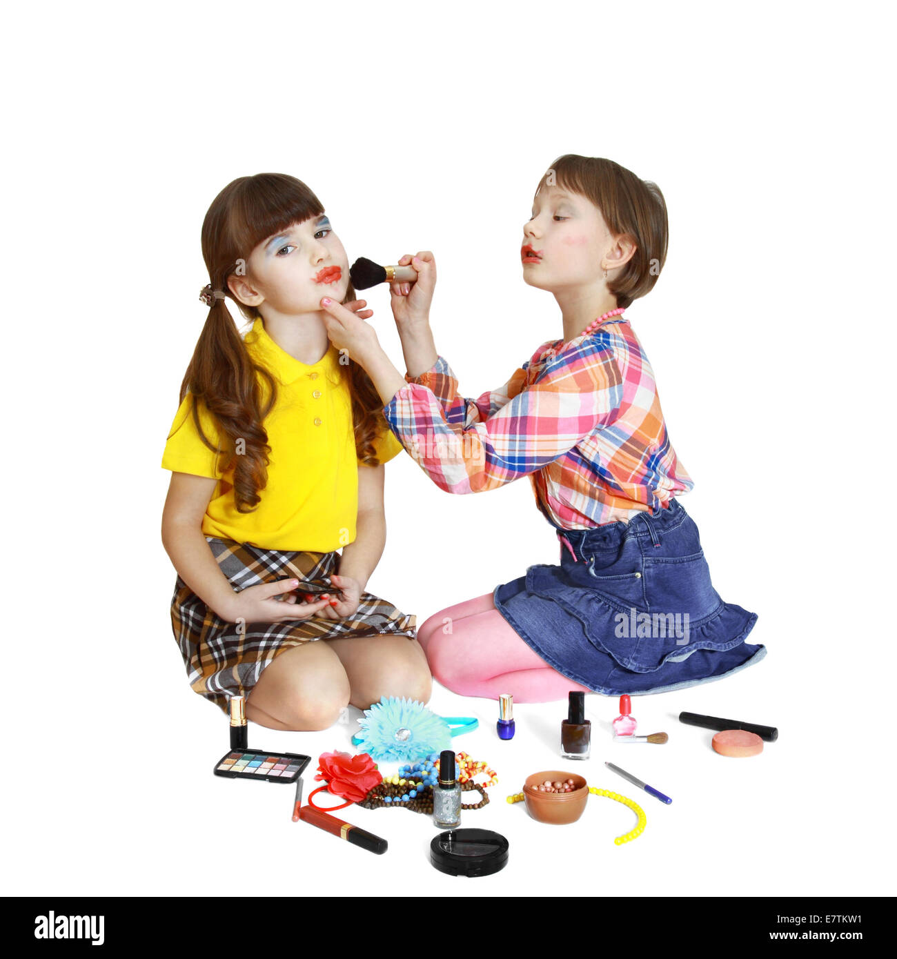 Two cute girls sit and play makeup on white background with shadows ...