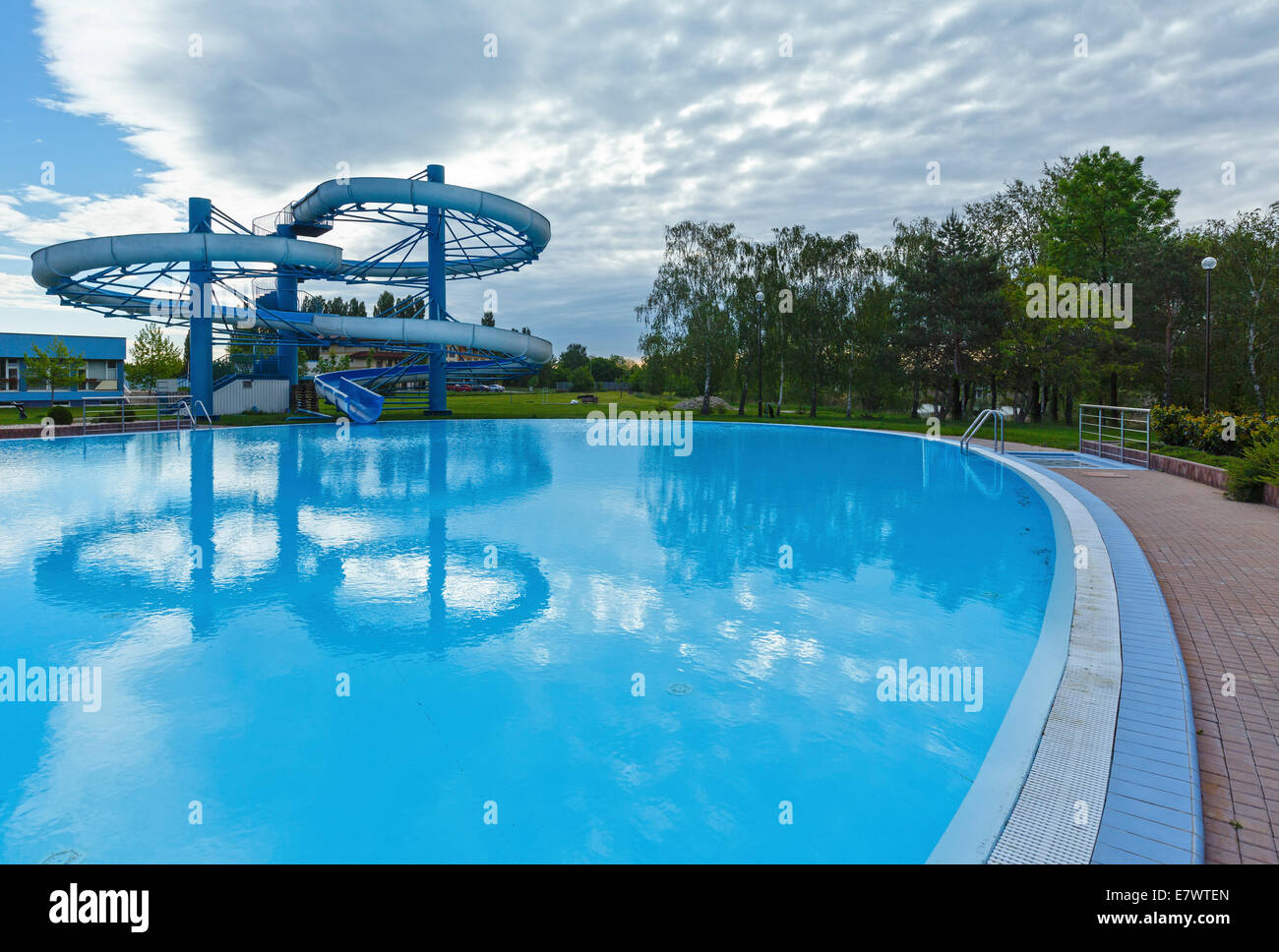 Outdoor swimming pool view with slide and trees reflection on water ...