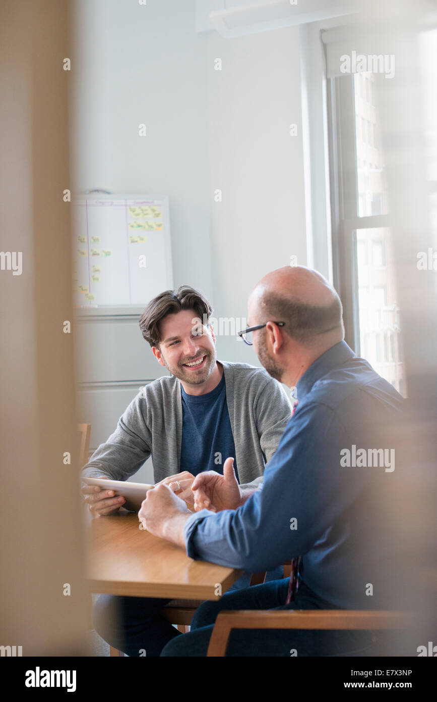 Two business colleagues in an office talking and referring to a digital ...