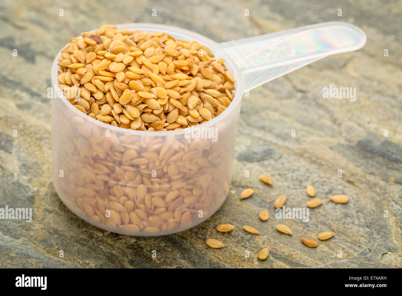 gold flax seeds in a measuring scoop against slate rock background ...