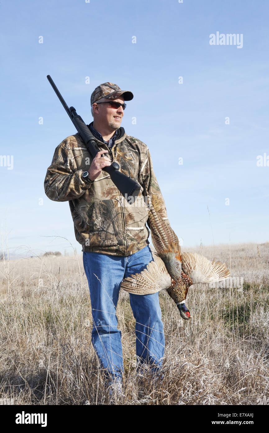 Hunter standing in field holding ring-necked pheasant and shot gun ...
