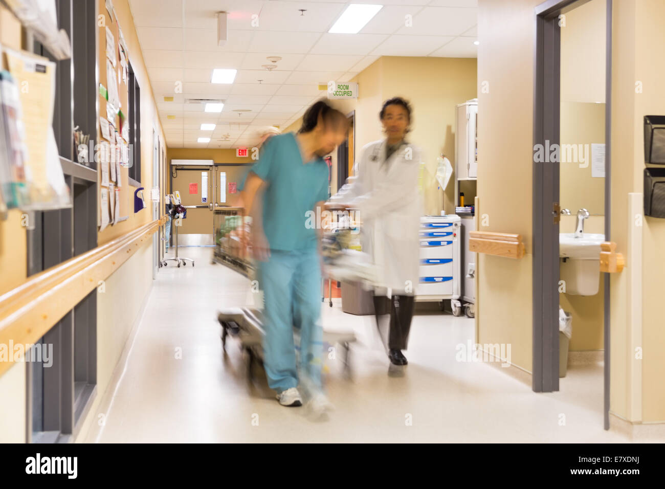 Full length of doctor and nurse pulling stretcher in hospital corridor ...