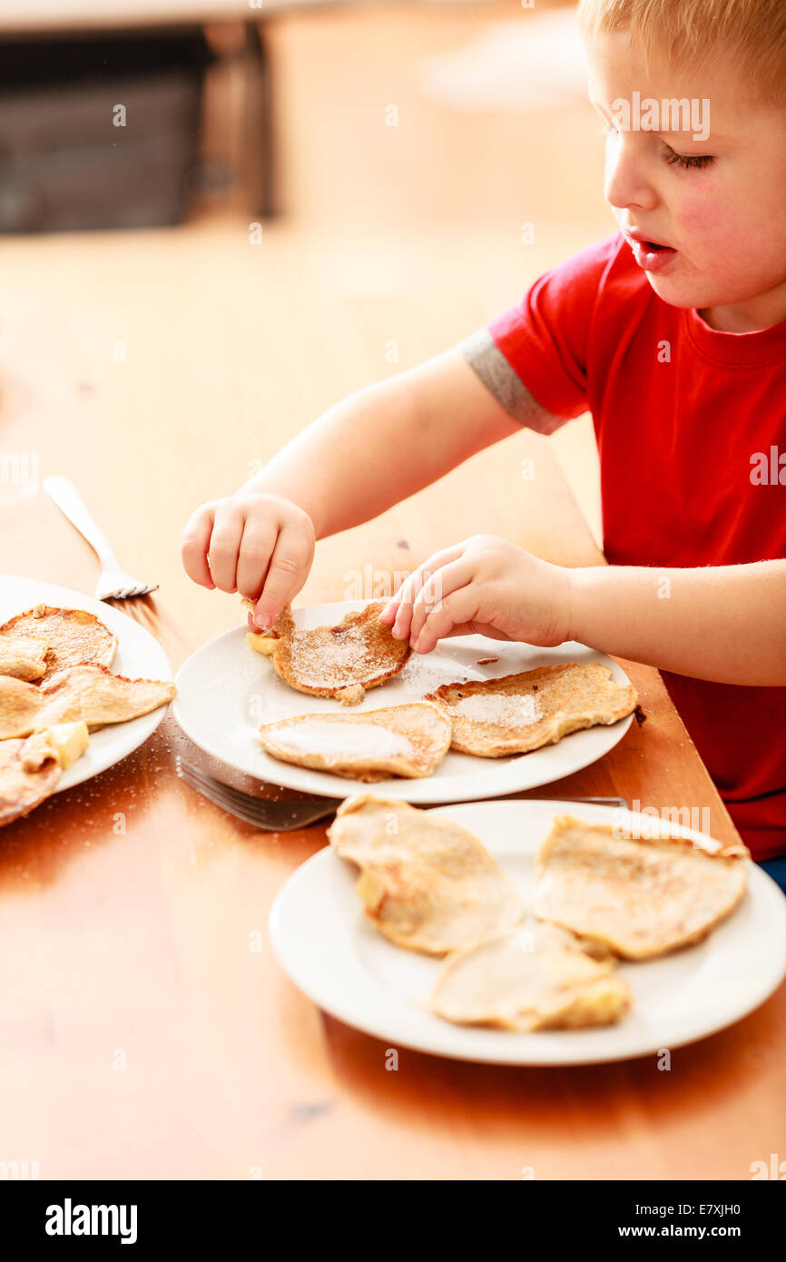 Little boy eating fried apple in pancake dough or apple fritters ...