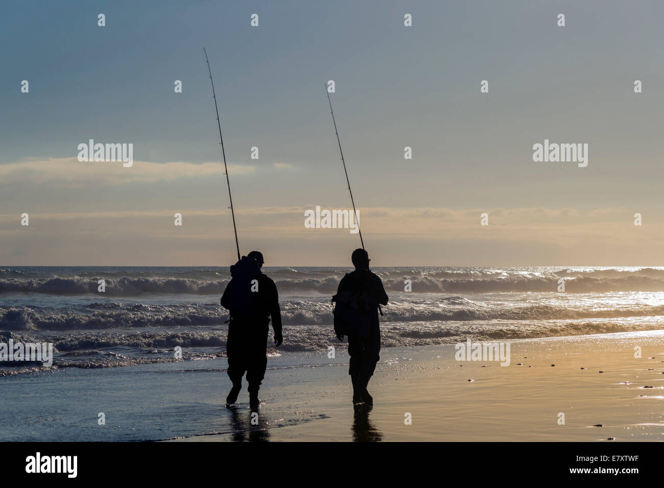 Two anglers walking with their fishing rods along the seaside beach ...