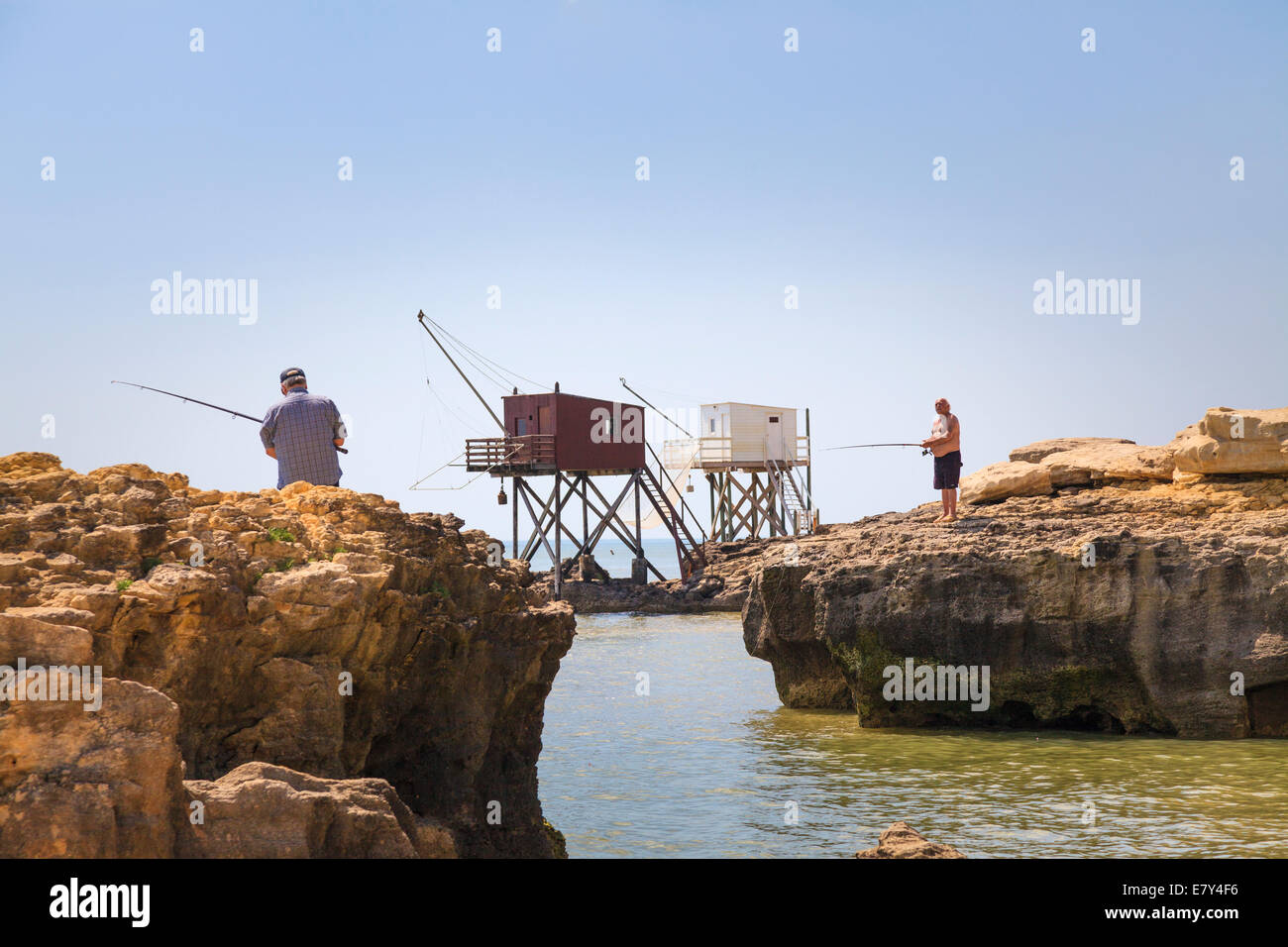 Two fisherman fishing off rocks with traditional fisherman huts on ...