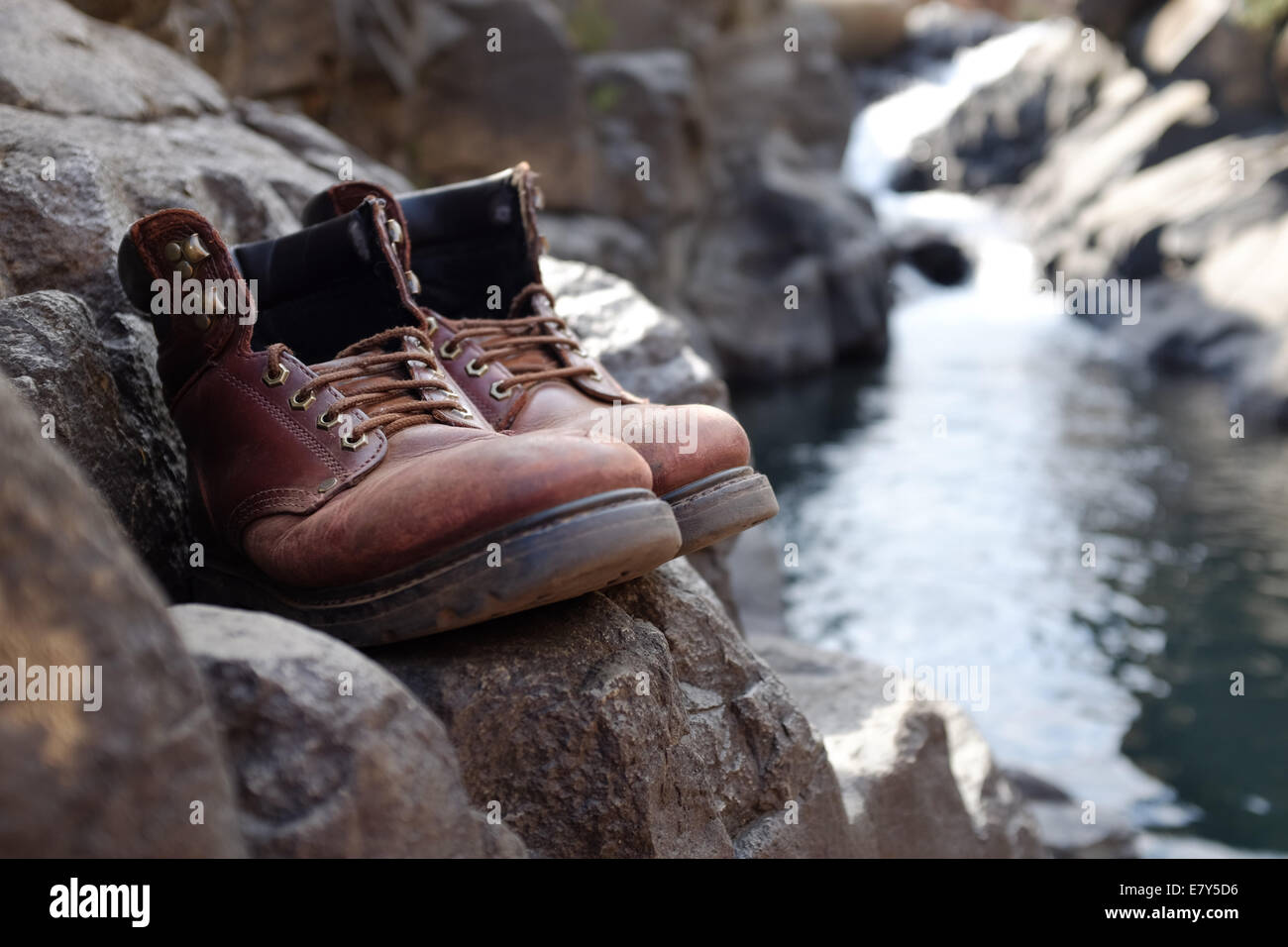 Limited focus hiking boots on rock with blurred river, stream ...