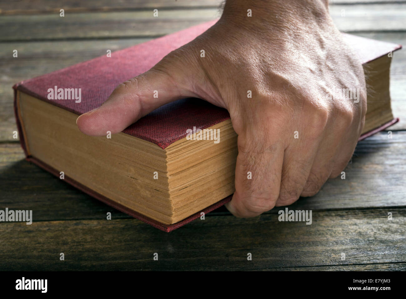 A man is resting his left hand on a red book at a table Stock Photo - Alamy