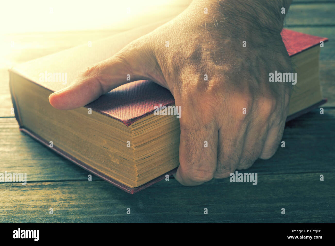 A man is resting his left hand on a red book at a table Stock Photo - Alamy
