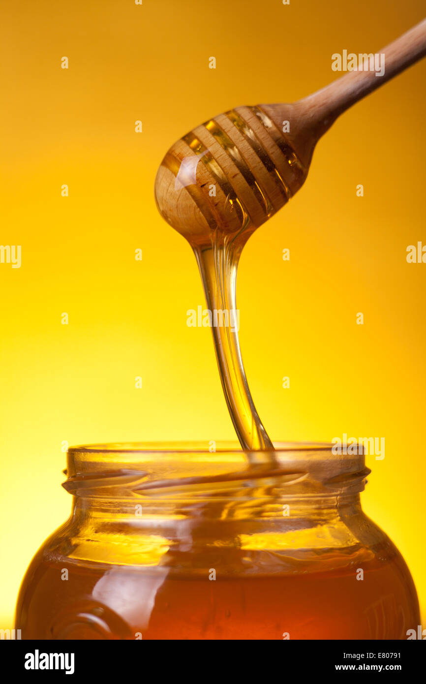 Close-up shot of wooden dipper with flowing honey over yellow ...