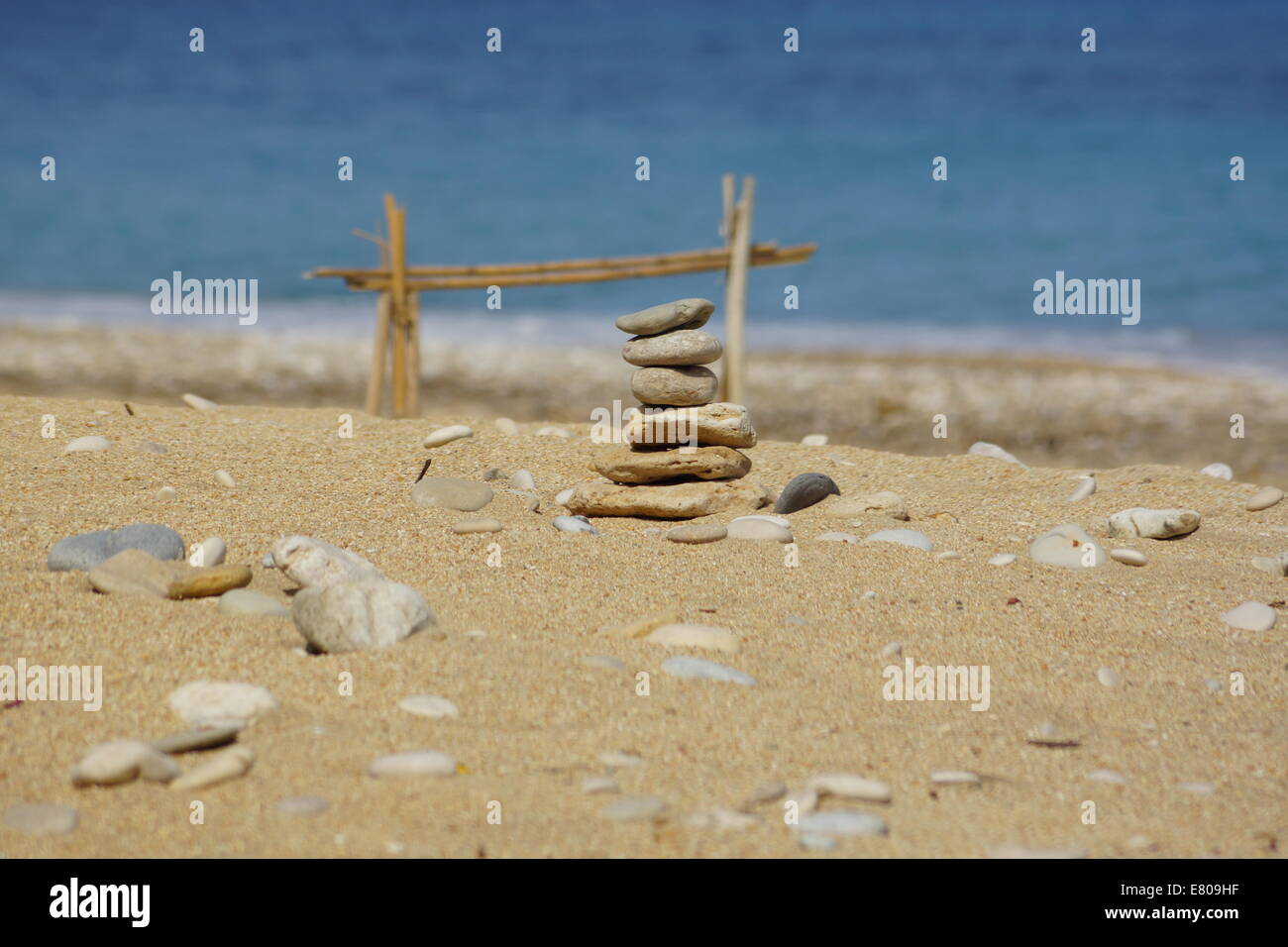 sandy beach scene, stone pile, wooden structure(roasting spit?) against ...