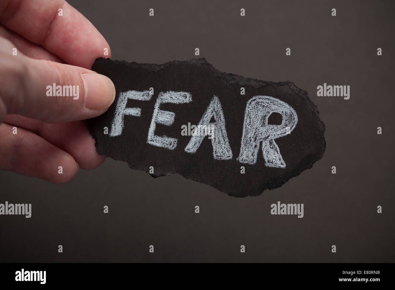 Black torn piece of paper with word "Fear" in hand against black ...