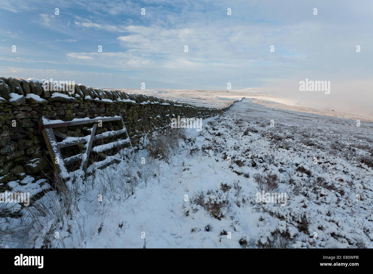 Drystone wall in winter, snow, blue sky, fog, old gate propped against ...