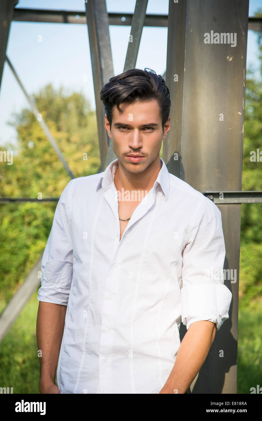 Handsome young man leaning against metal electricity trellis, looking ...