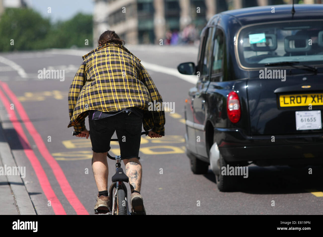 Rear view of a cyclist riding over Waterloo Bridge next to a taxi in a ...
